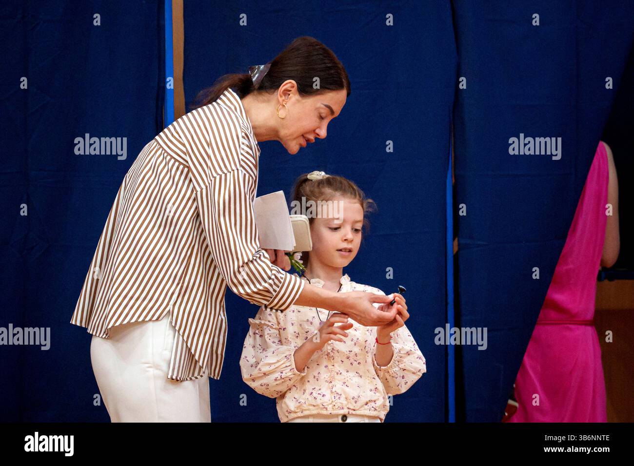 A woman hands a little girl a voting stamp after exiting a voting booth ...