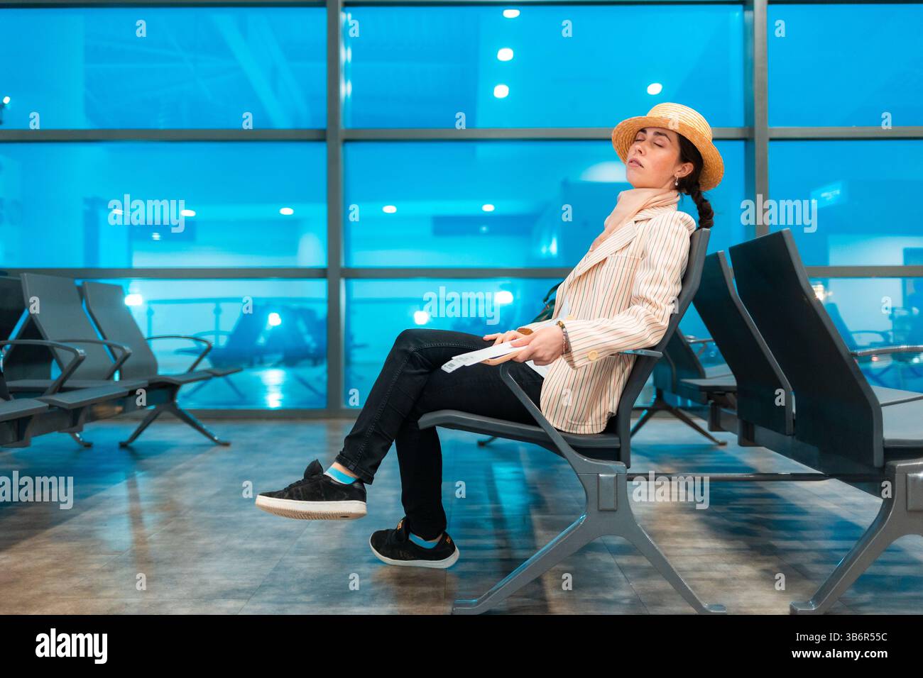 Side view of young Caucasian elegant tired woman sitting on chair at waiting airport area and ...