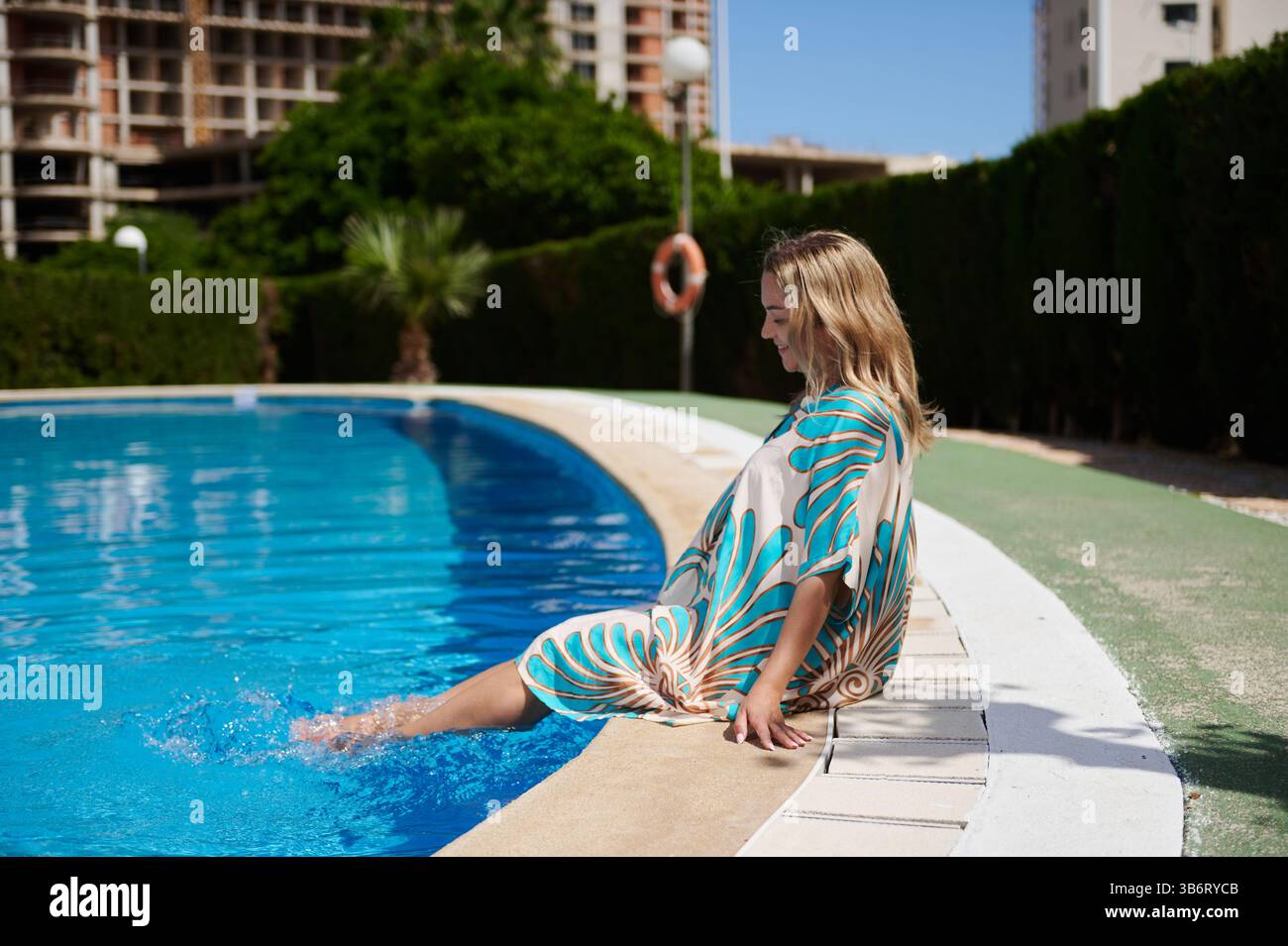 A serene scene featuring a woman sitting by a clear blue pool, dipping ...