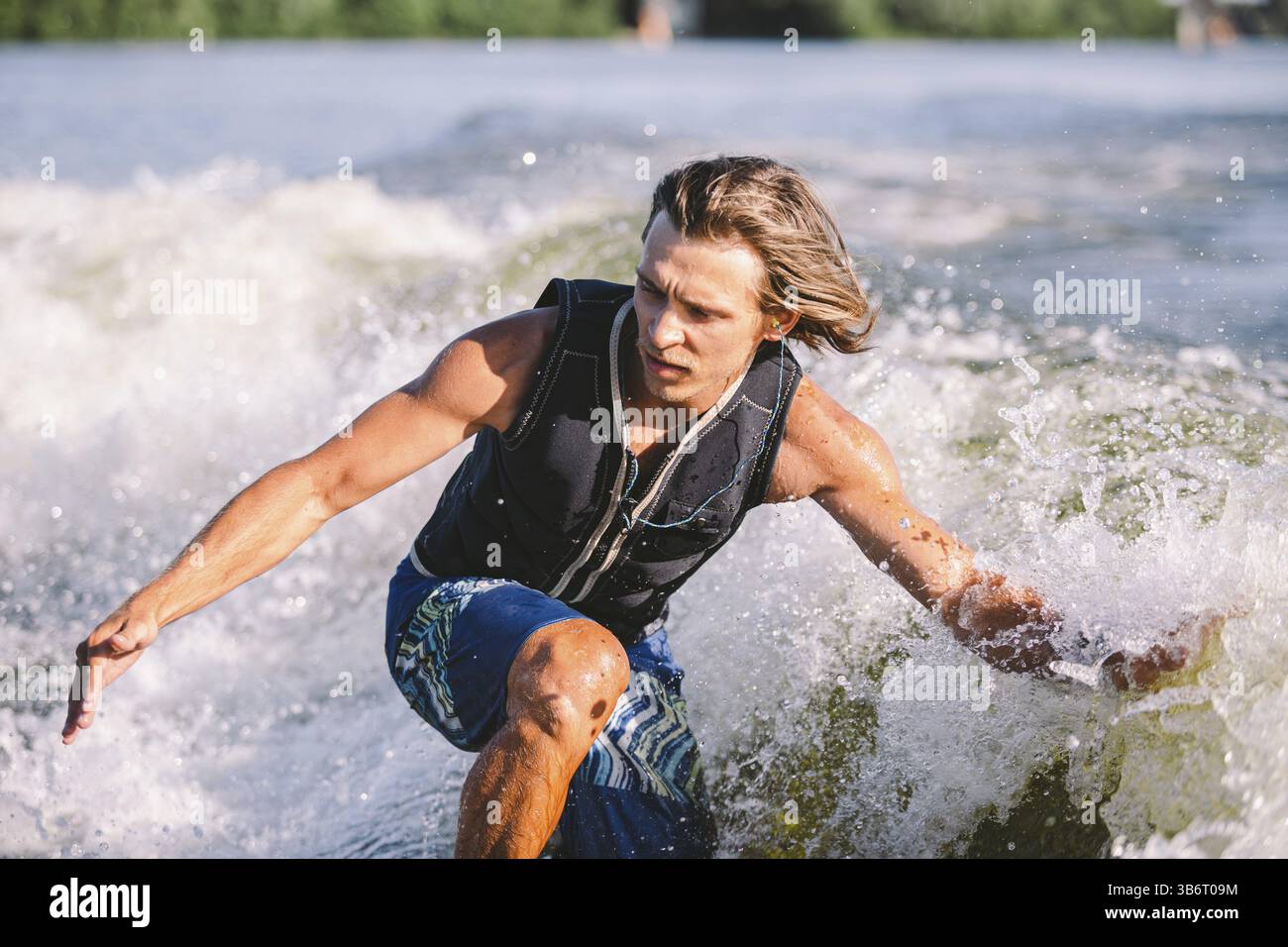 Beautiful long haired blond wakesurf in vest on board along waves of ...