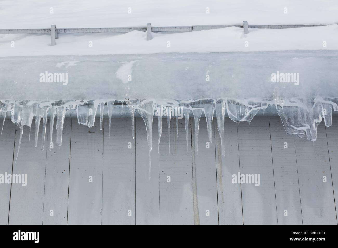 Icicles and thick heavy ice hanging from roof edge of grey wood plank ...