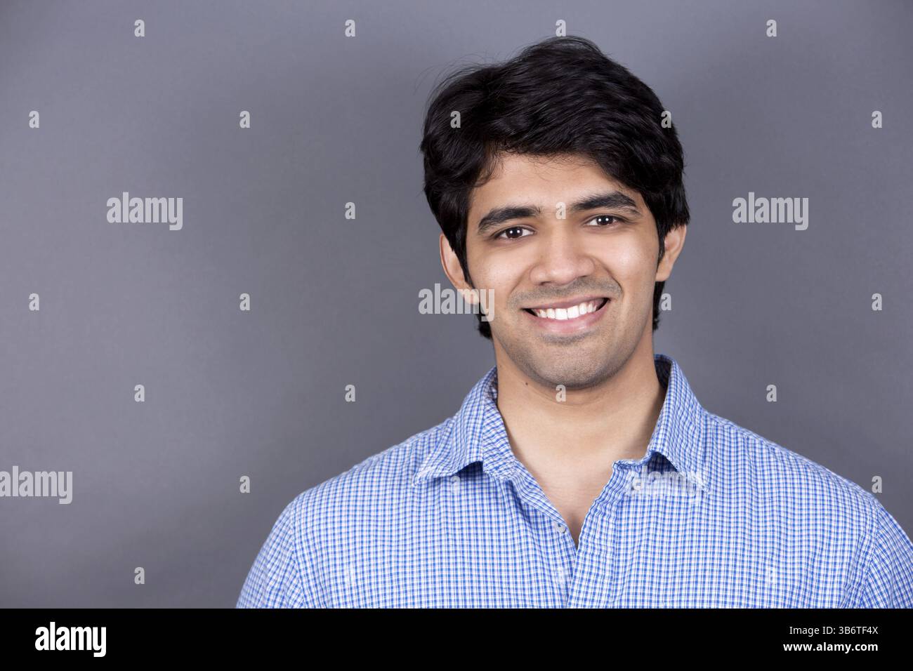 Handsome east indian man wearing blue shirt on light grey background ...