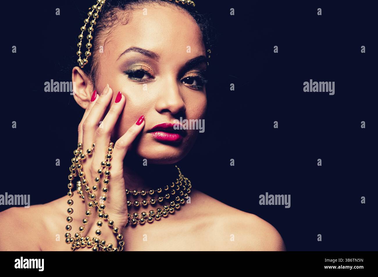 Upscale Indian woman wearing gold jewellery and red lipstick on dark ...