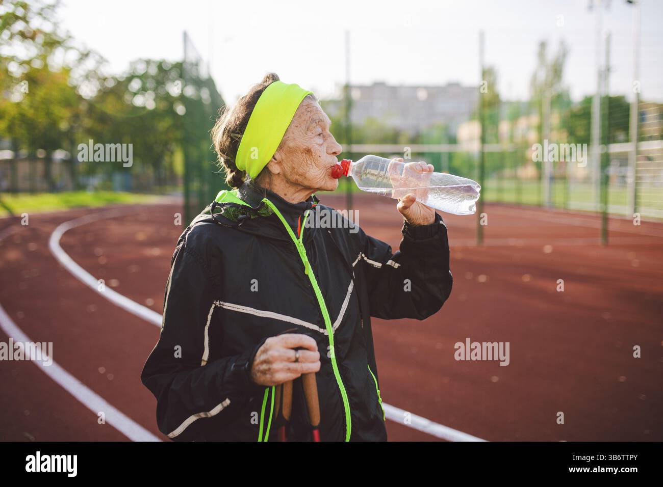 Old woman walking with nordic walk sticks on running track, rubber ...