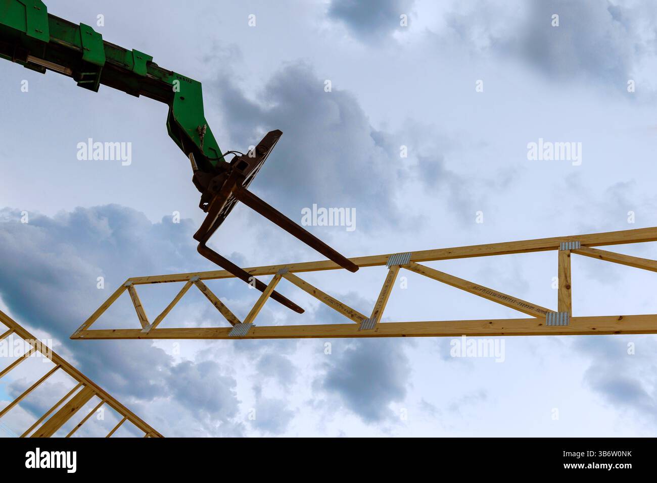 Telehandler machine at construction site lifts wooden truss into place ...