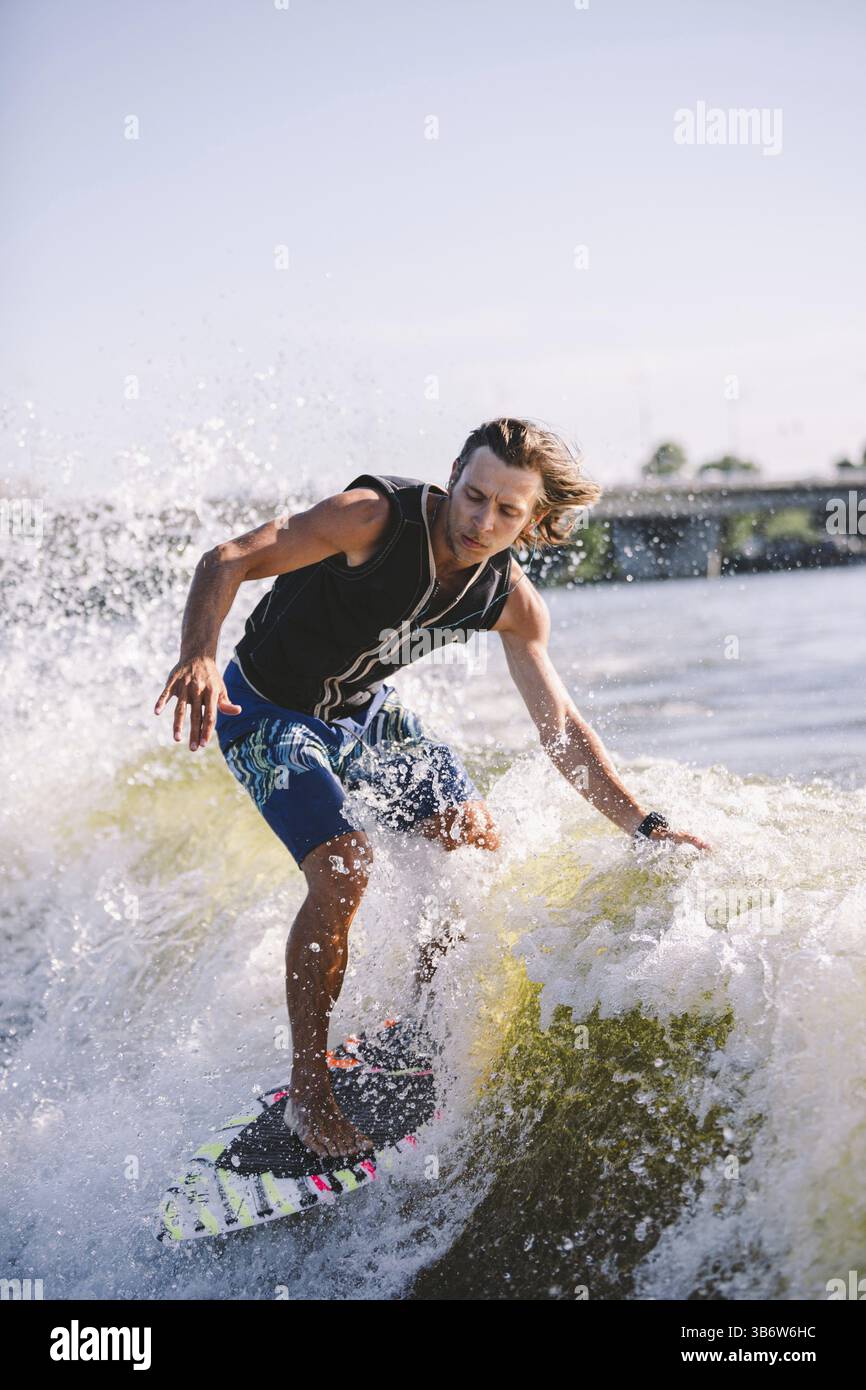 Beautiful long haired blond wakesurf in vest on board along waves of ...