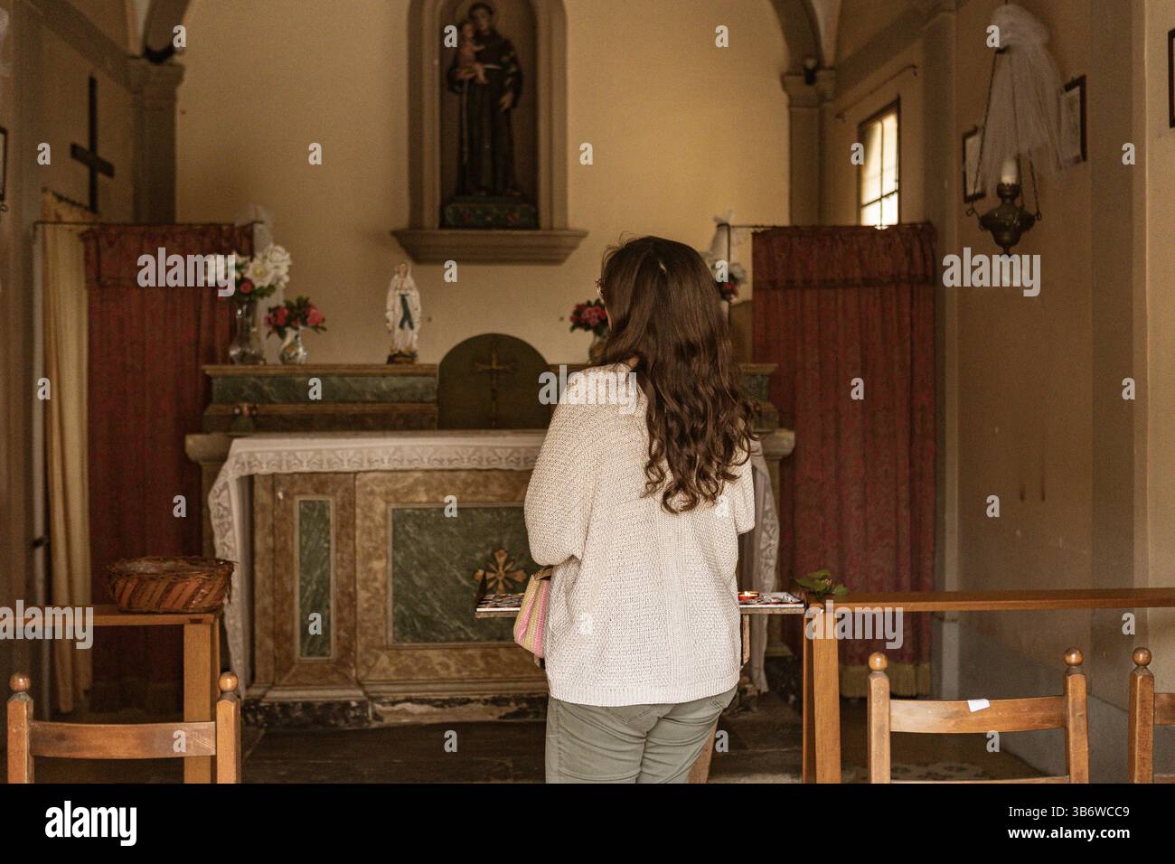 Tourist visiting a small italian church, admiring the altar and praying ...