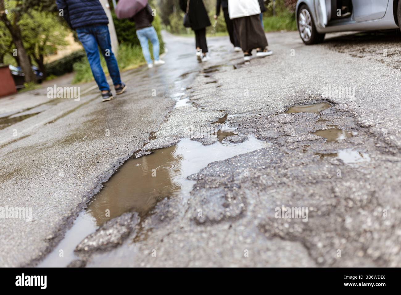 Tourists walking on a damaged asphalt road with potholes and puddles ...