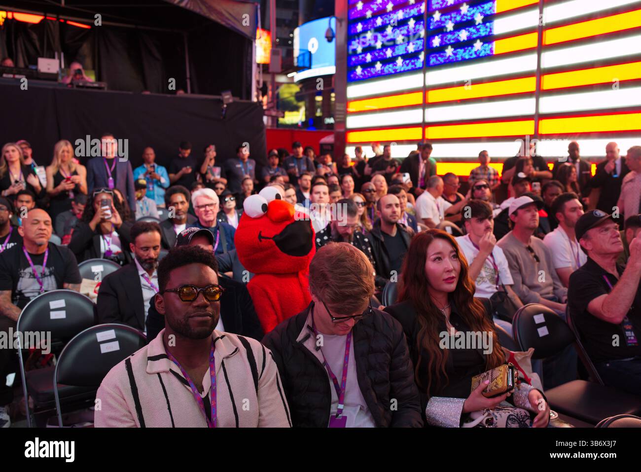 An outdoor audience sits before a large American flag LED display. A ...
