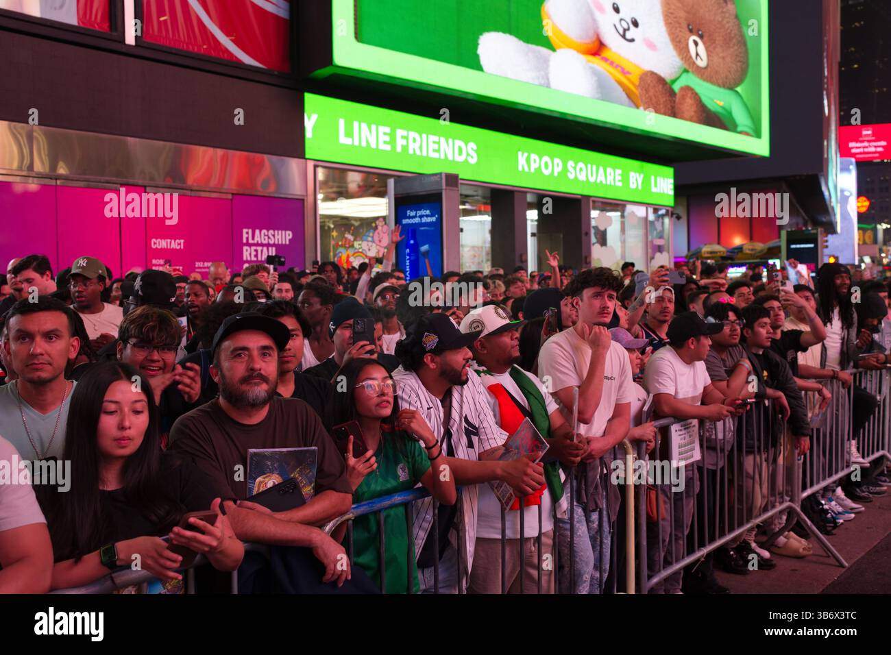 A large crowd of people stand behind a metal barricade in front of a ...