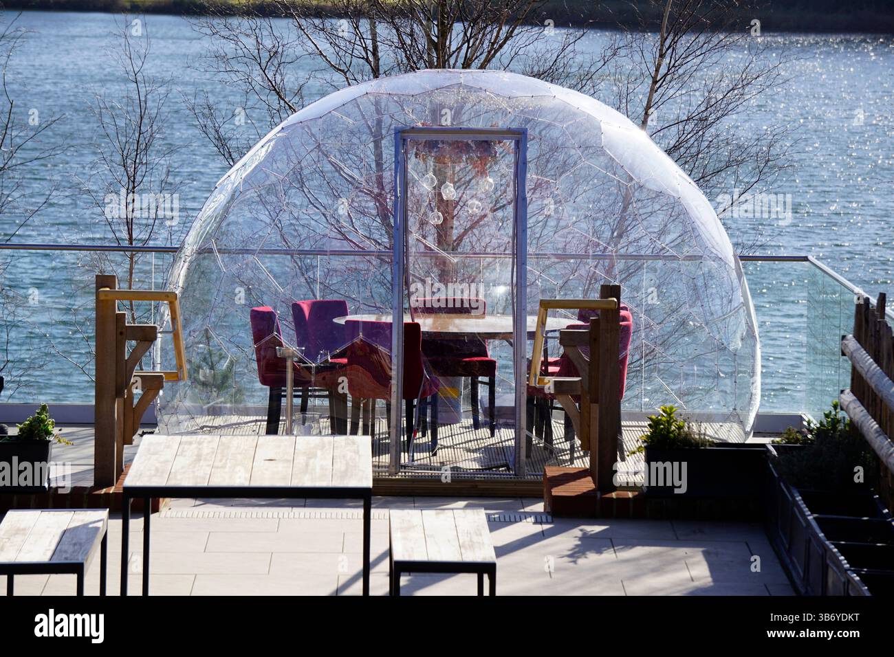 Transparent igloo dining pod with a lakeside view on a sunny terrace ...