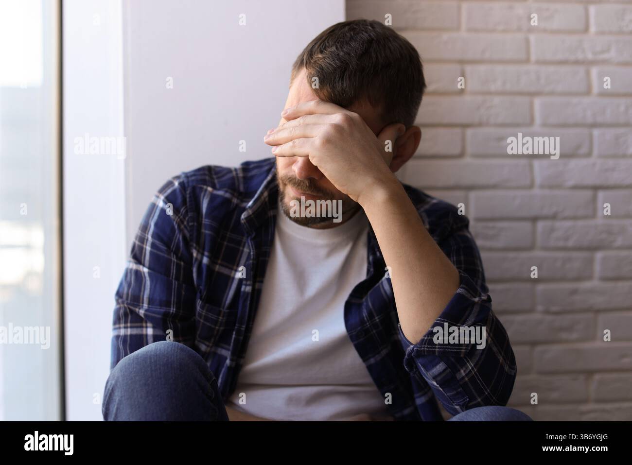 Depressed man sitting near window at home Stock Photo - Alamy