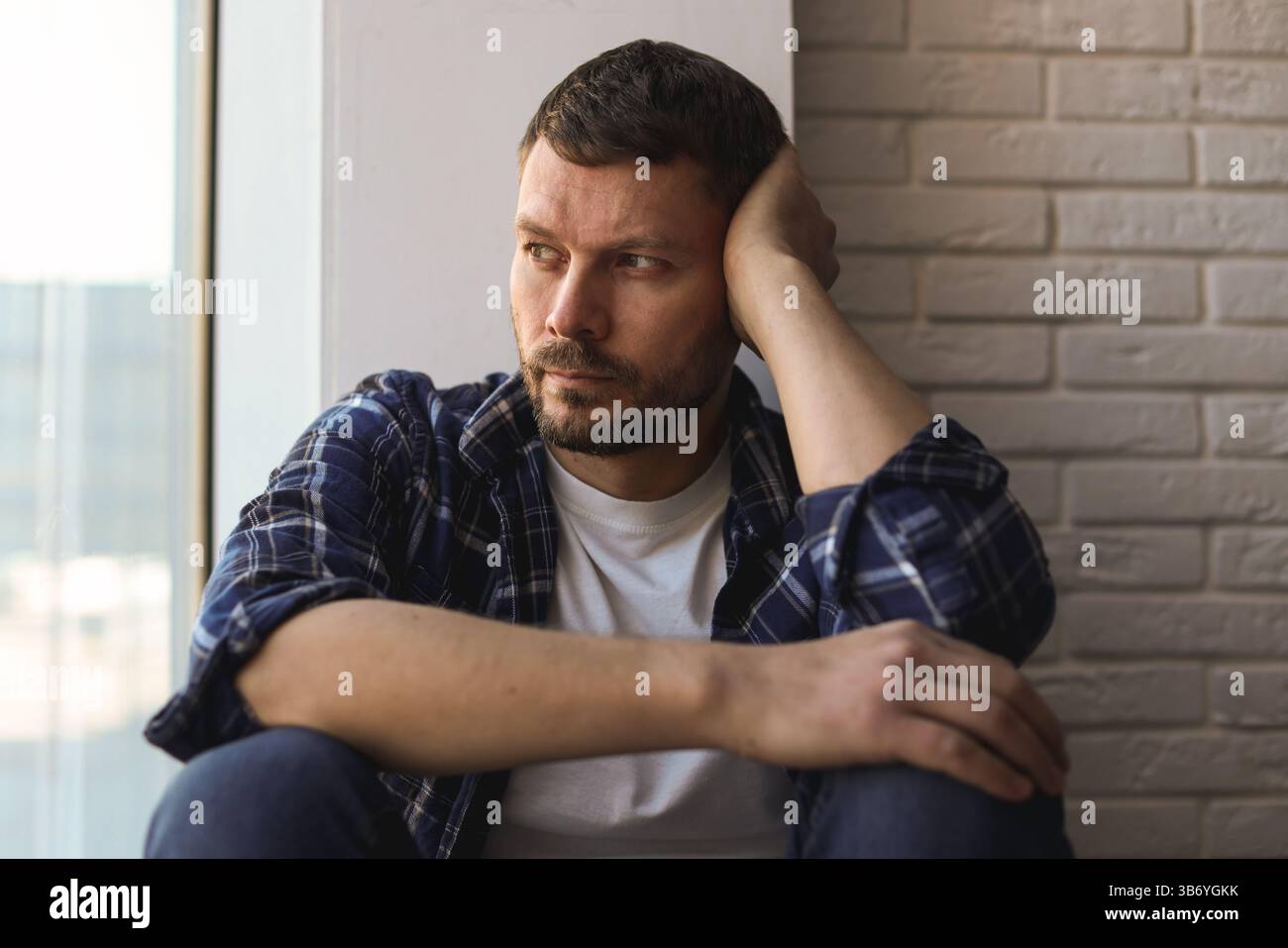 Depressed man sitting near window at home Stock Photo - Alamy
