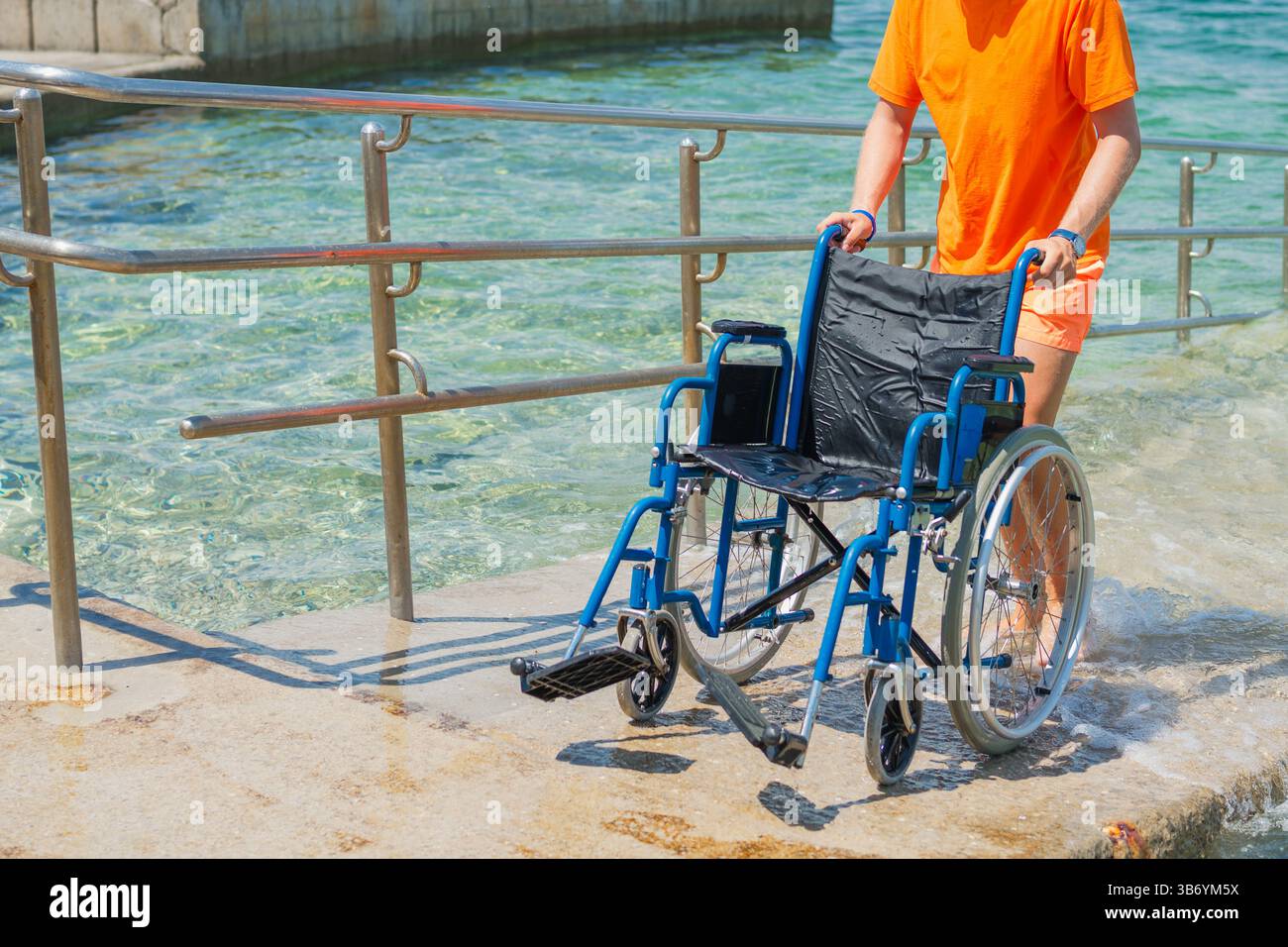 Lifeguard rolling an empty aquatic wheelchair along an accessible beach ...
