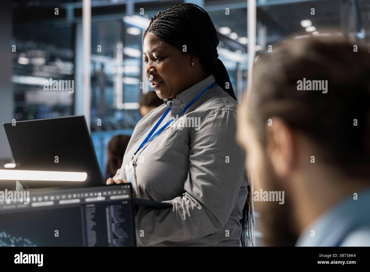 Technician using laptop to oversee server infrastructure powering algorithm training and data ...