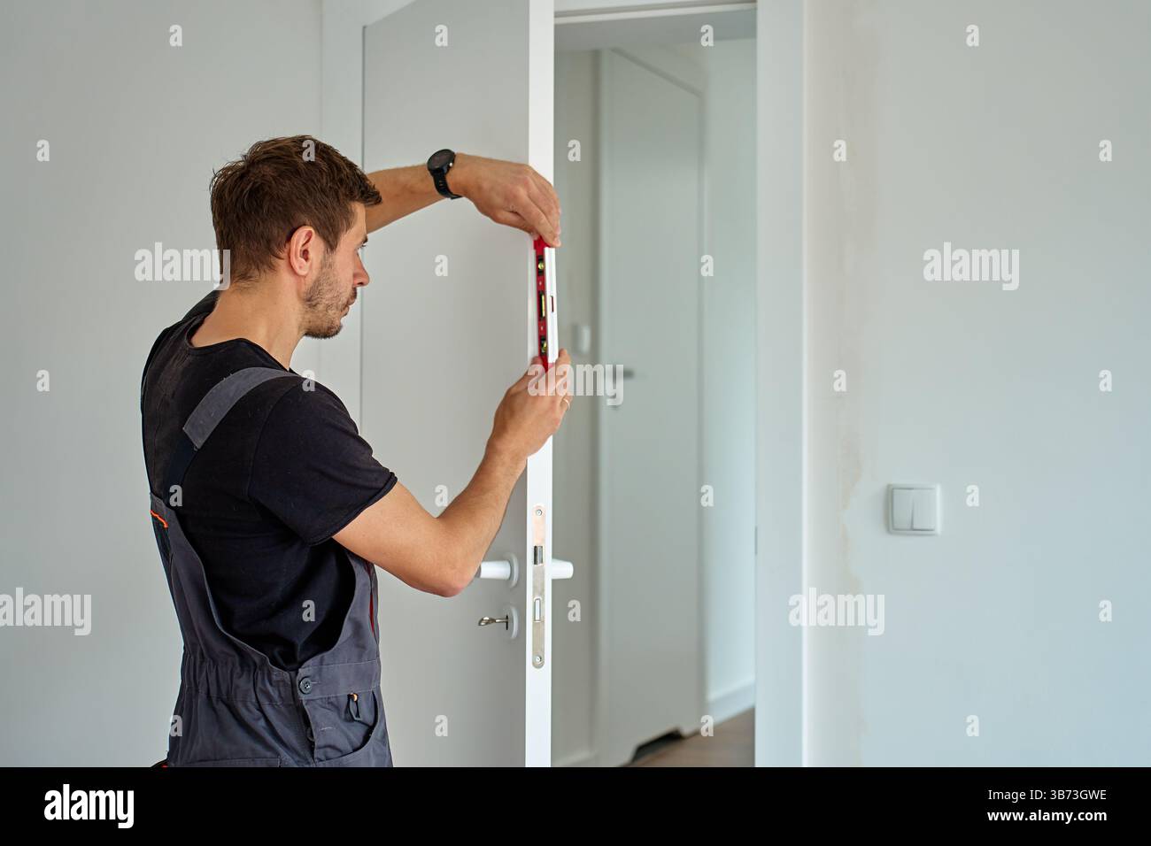 Worker checking vertical alignment of door with bubble level ...