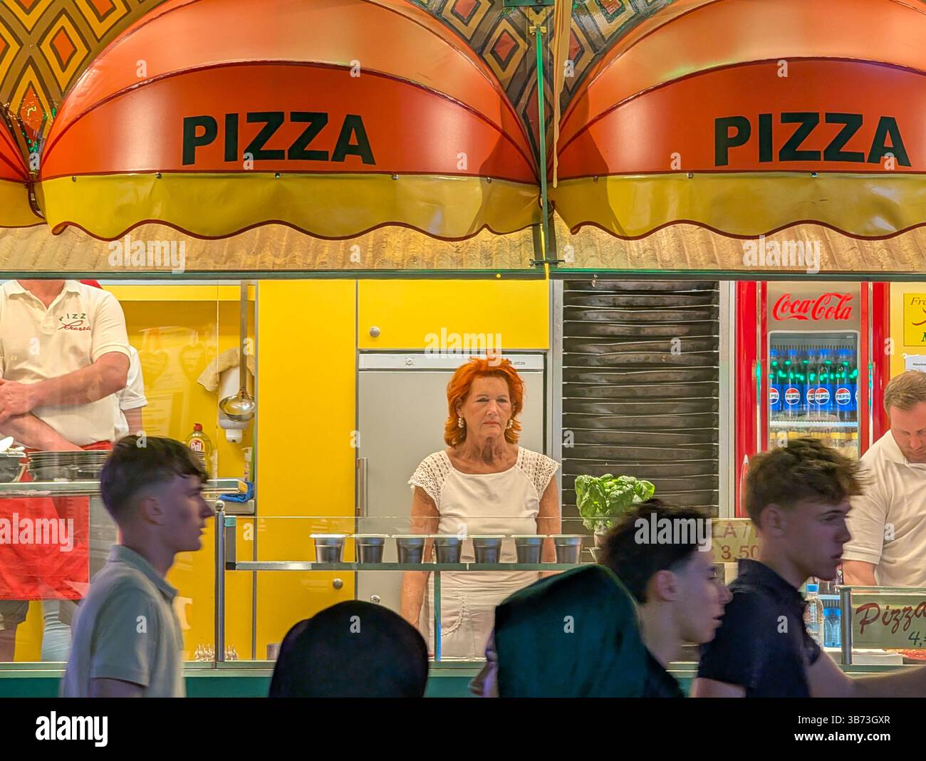 Workers prepare and serve pizza at a brightly lit food stand during a ...