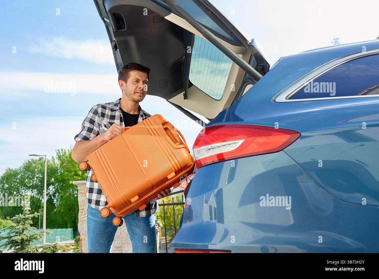 Man loading orange suitcase into car trunk before journey. Packing ...