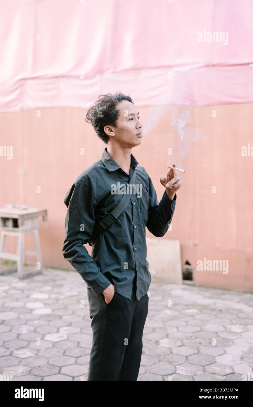 Relaxed young man enjoying a cigarette outdoors. He is standing in a ...