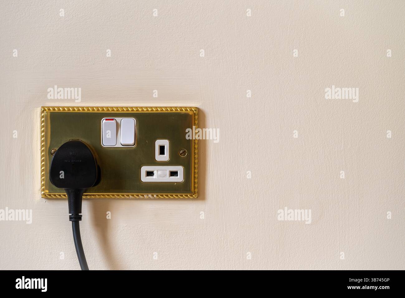 UK style double electrical socket with plug inserted. Gold socket with ...