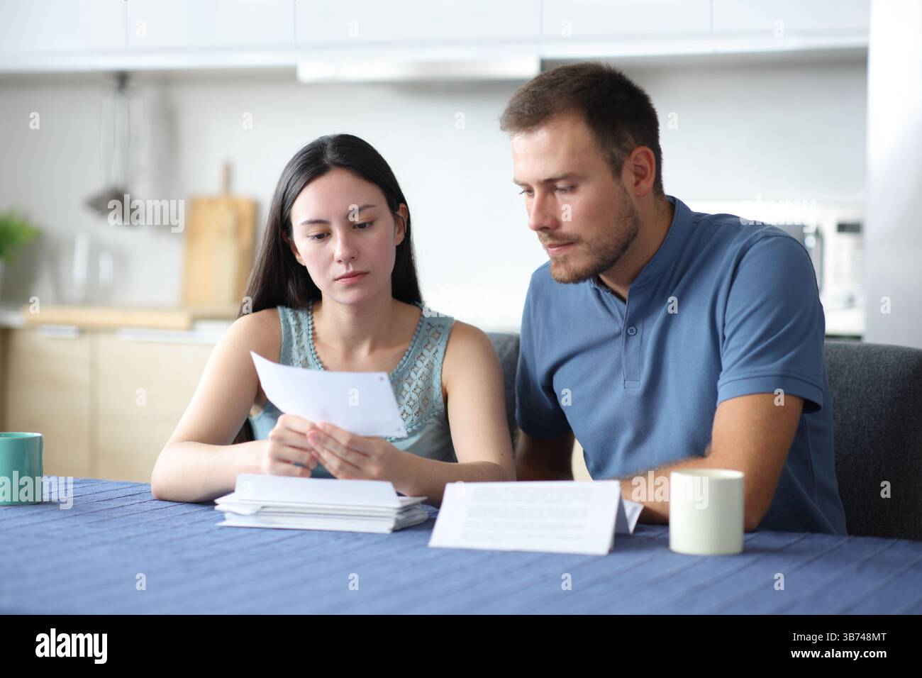 Serious interracial couple reading bank letter in the kitchen at home ...
