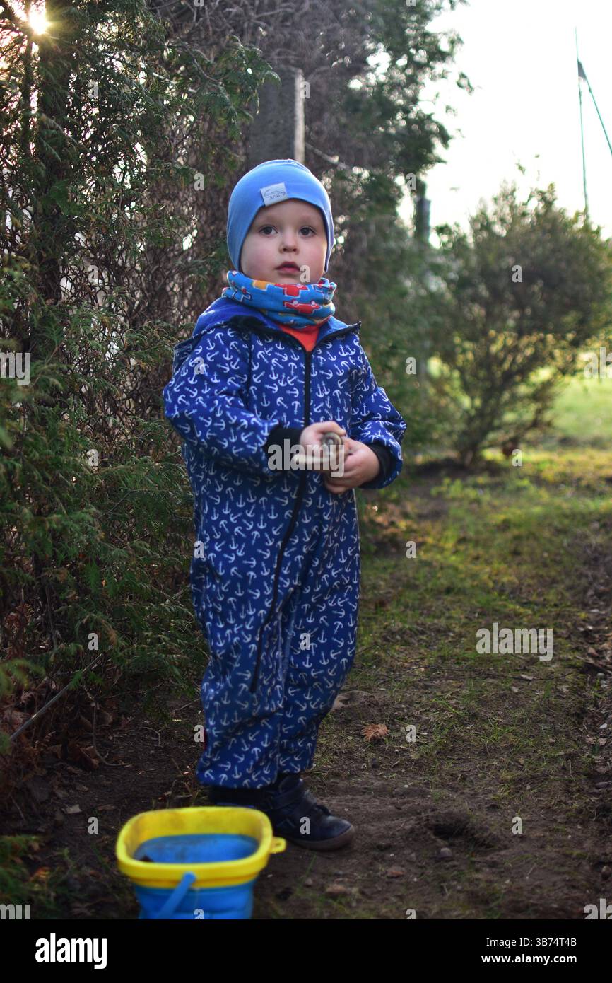 Toddler boy in blue soft shell bodysuit is playing with garden hoe ...