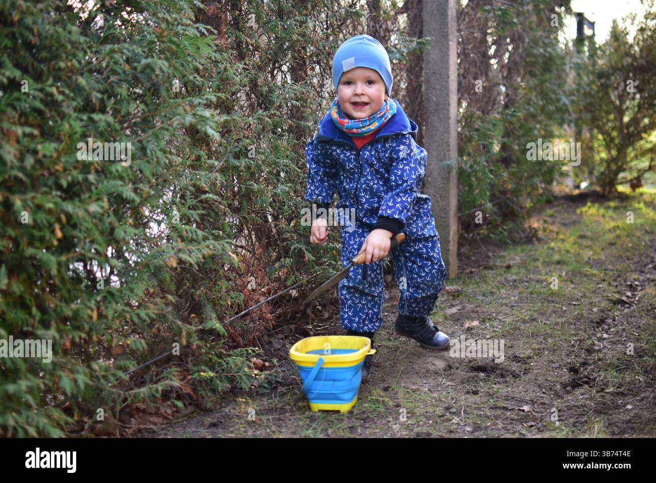 Toddler boy in blue soft shell bodysuit is playing with garden hoe ...