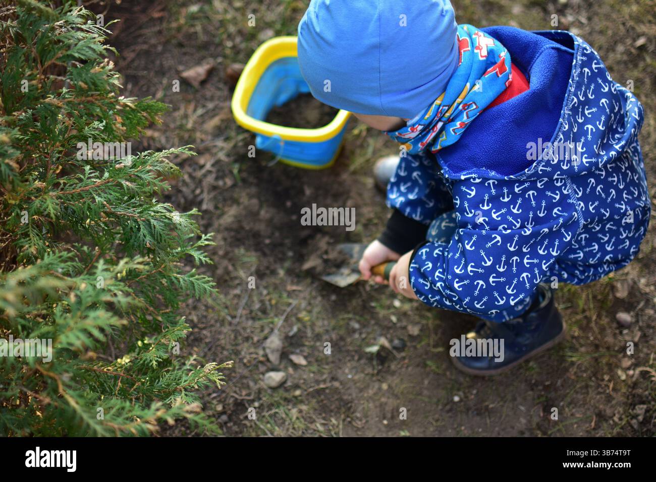 Toddler boy in blue soft shell bodysuit is playing with garden hoe ...