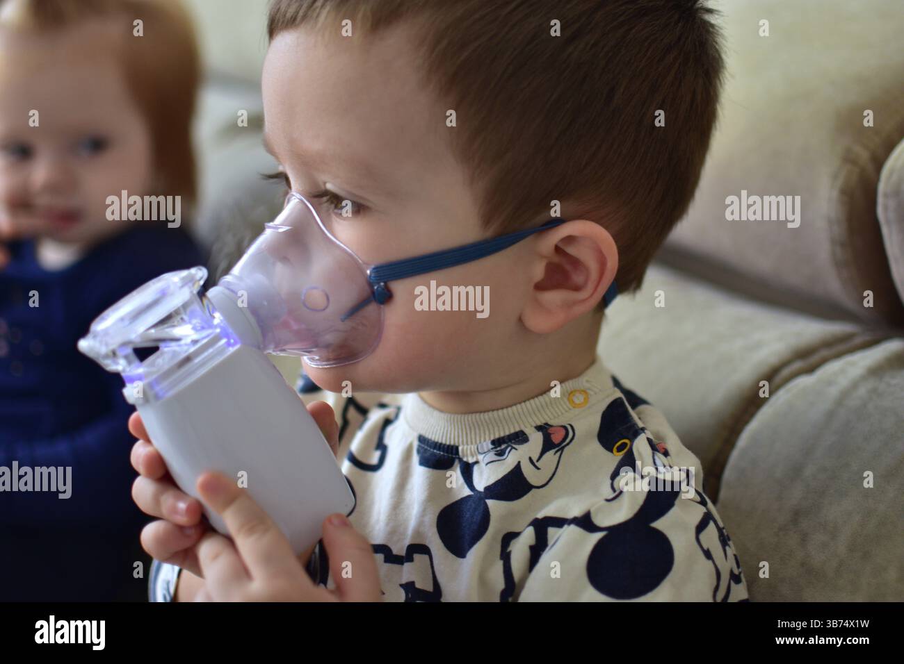 Sick toddler boy is using small nebuliser inhaling air. Kid breathing ...
