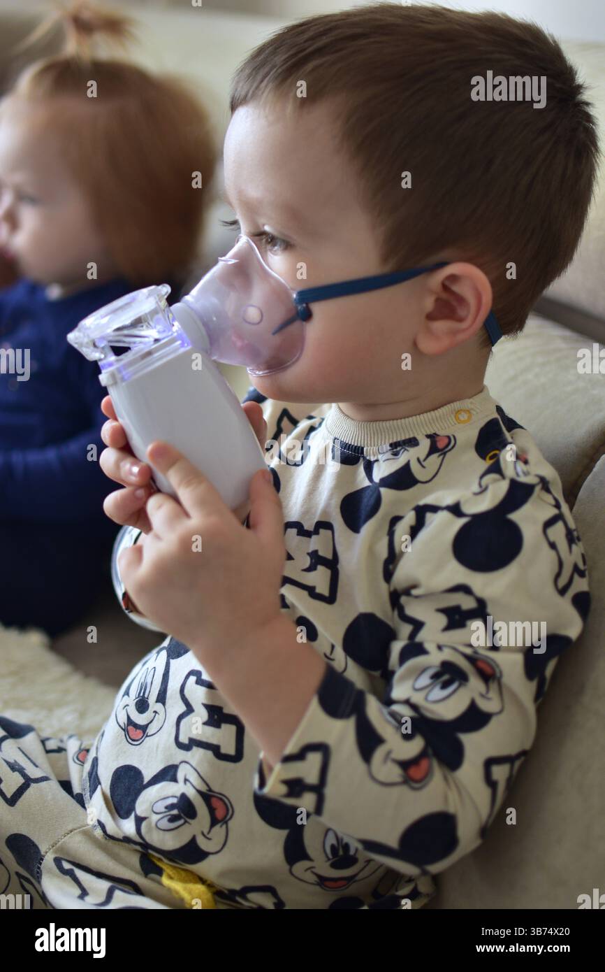 Sick toddler boy is using small nebuliser inhaling air at home. Kid ...