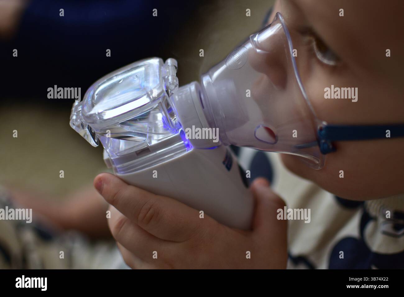 Sick toddler boy is using small nebuliser inhaling air. Kid breathing ...