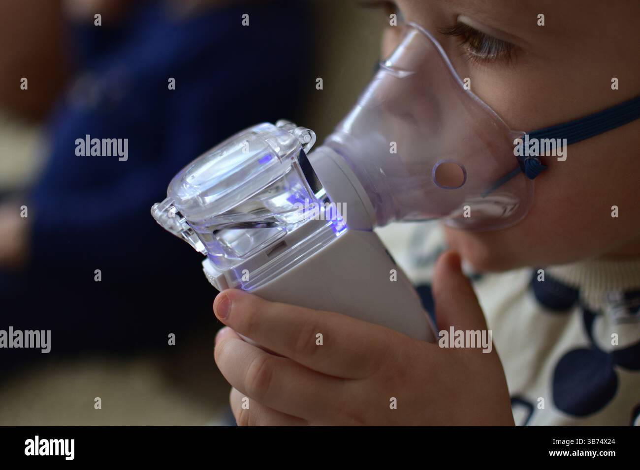 Sick toddler boy is using small nebuliser inhaling air. Kid breathing ...