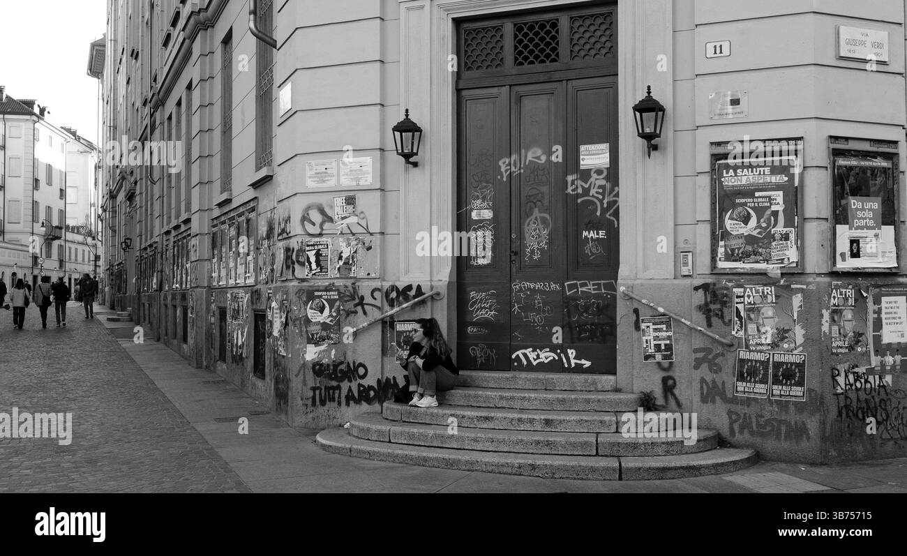 Girl sitting on steps of a building covered in protest graffiti, Turin ...