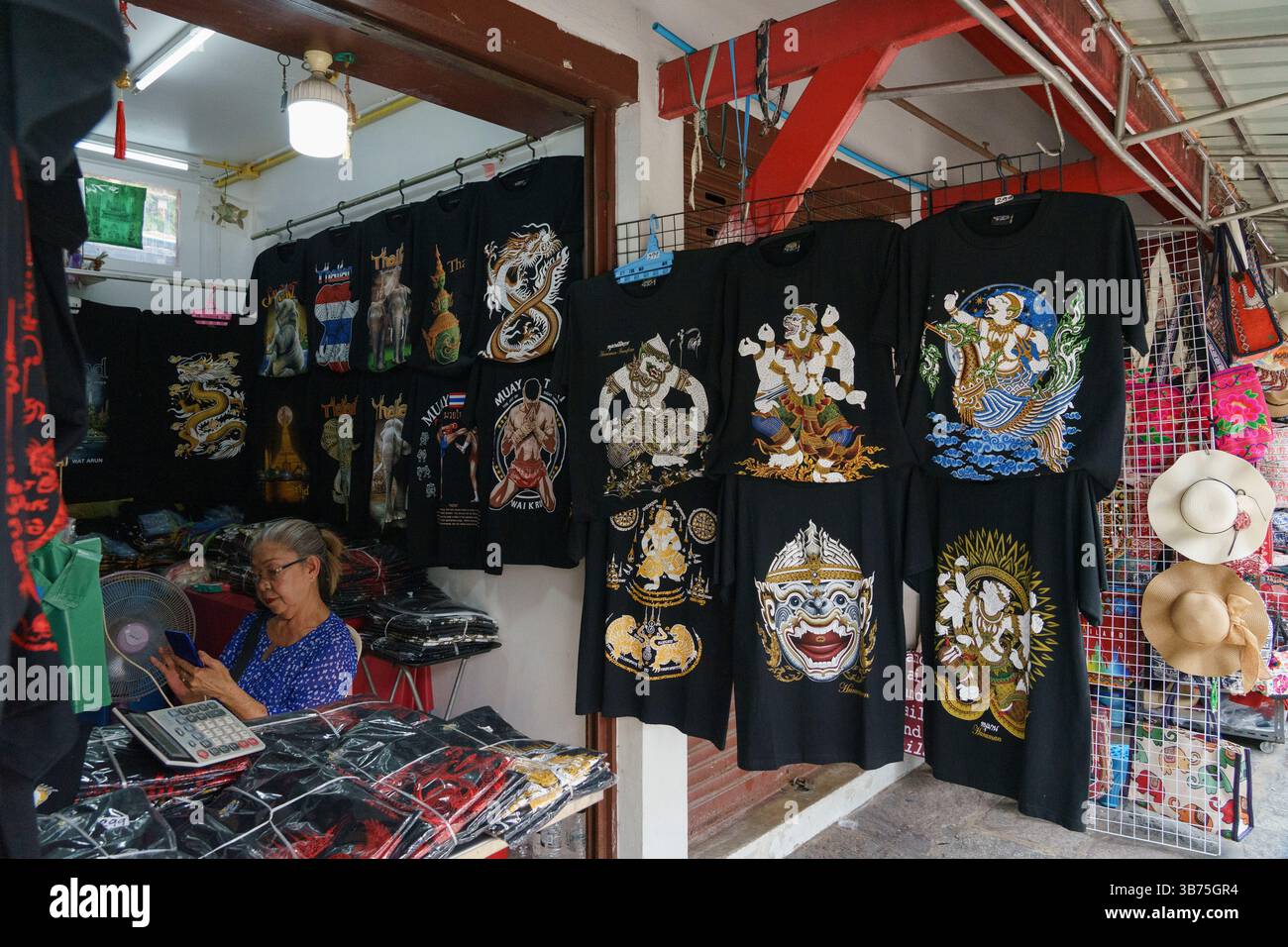 Bangkok, Thailand. 5th May, 2025. A vendor is sitting inside a souvenir store with shirts ...