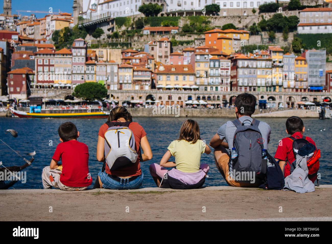 Family back view sitting on embankment of river Douro, Porto. Tourists ...