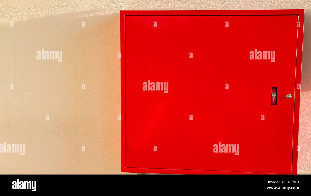 Vibrant red metal box on light beige wall with shadow play highlights ...