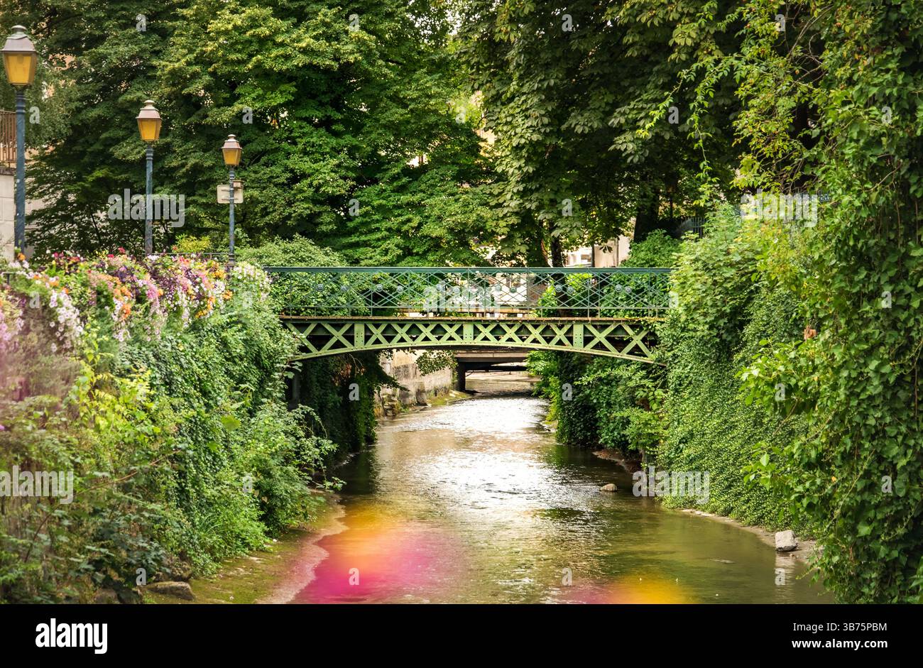 Green pedestrian bridge over canal with flowers and classic French ...
