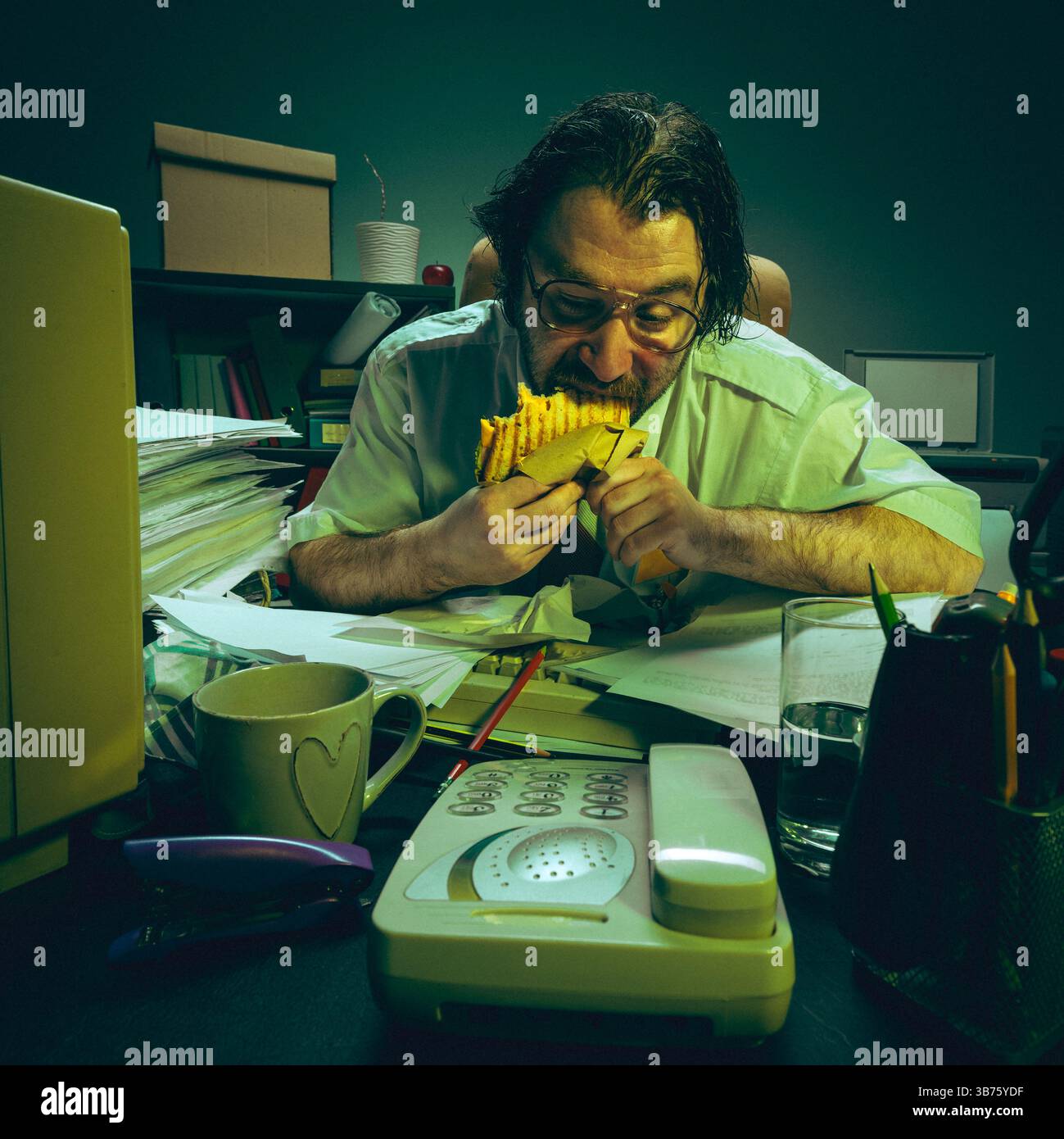 Worker eats sandwich aggressively at desk while buried in paperwork ...
