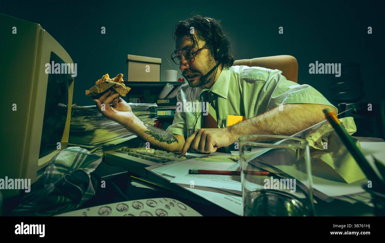 Office worker with headset eats sandwich while working at messy desk in ...