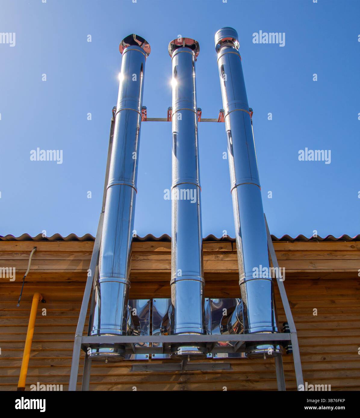 Shiny chimney and ventilation pipes coming out of the wall of the house ...
