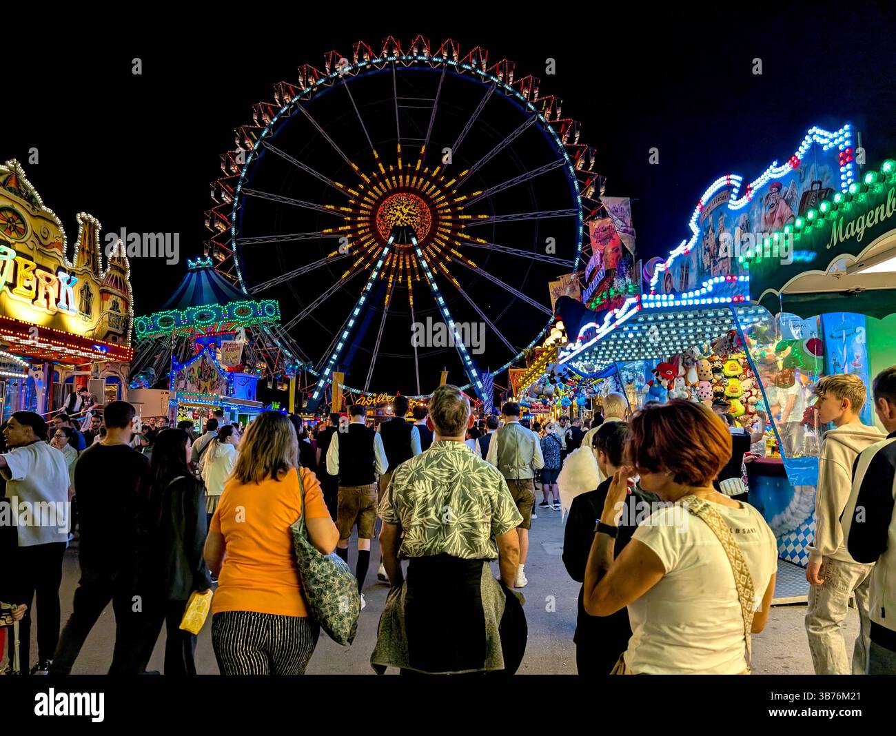 A large crowd strolls through a brightly illuminated fun fair with a ...