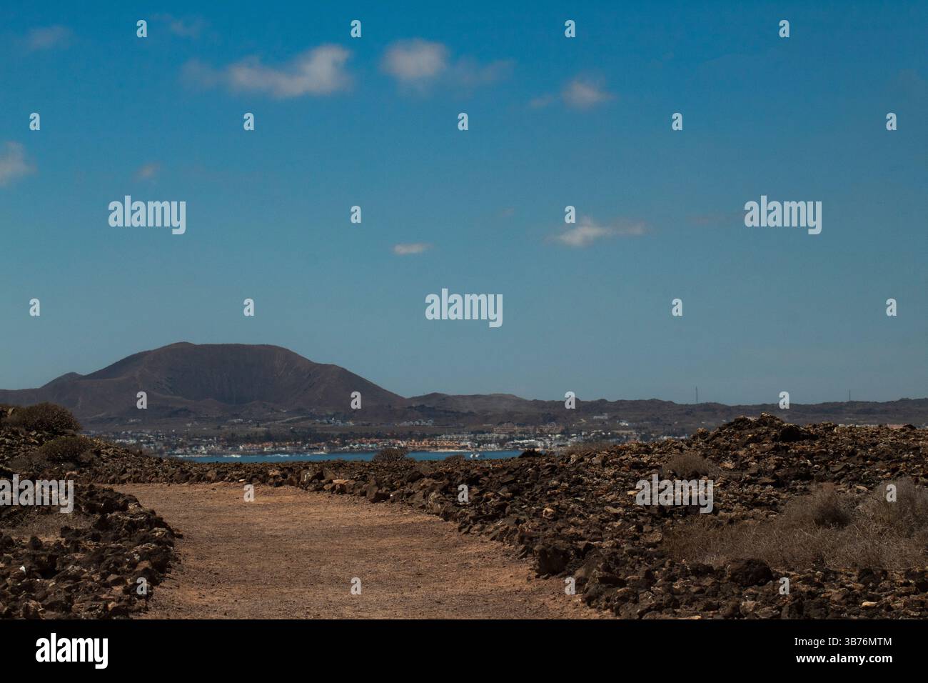 A natural pathway cuts through volcanic terrain and leads toward a ...