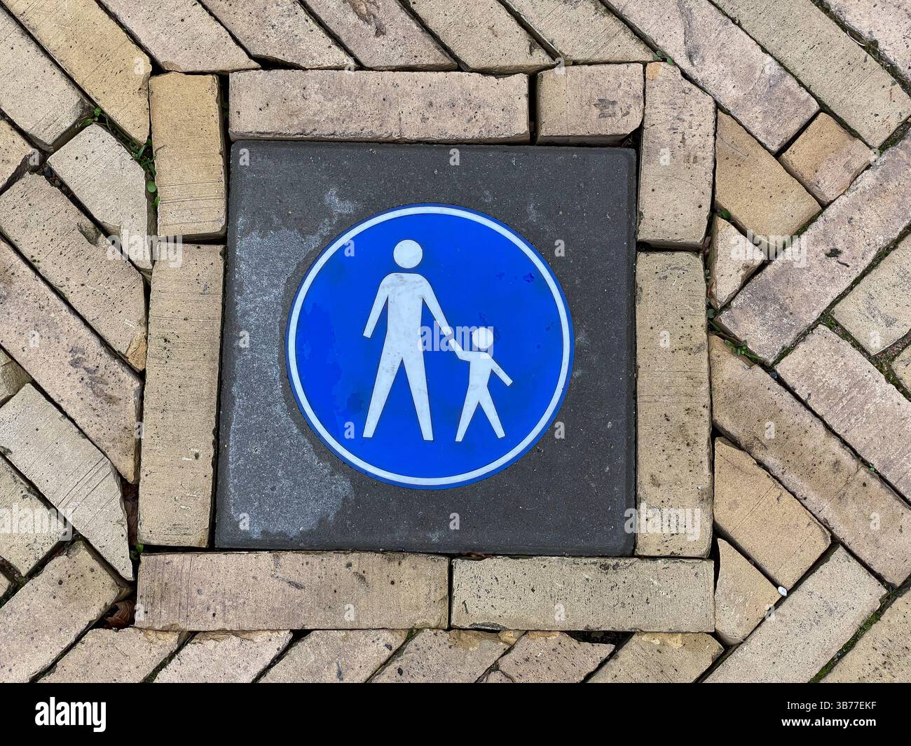 A pedestrian sign embedded in a walkway, featuring a blue circular ...
