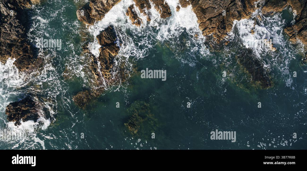 A dangerous sea wave crashes into the rocky coast with spray and foam ...