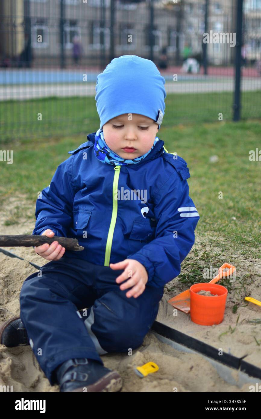 Toddler boy is playing with a bucket and a shovel in sandbox in a back ...