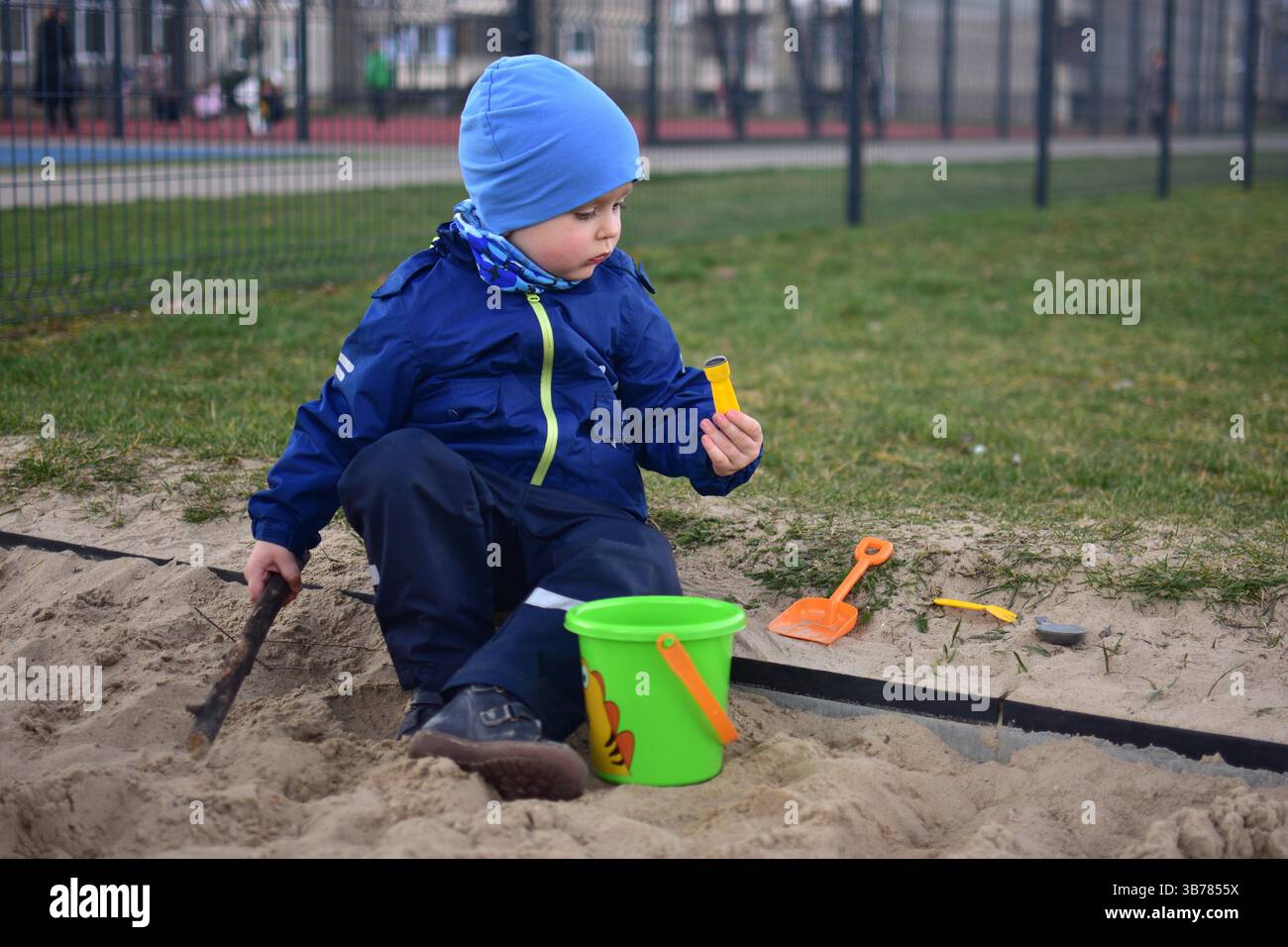 Toddler boy is playing with a bucket and a shovel in sandbox in a back ...