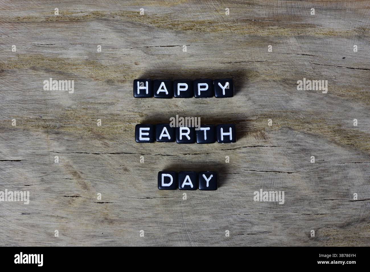 Greetings happy earth day made of black plastic beads on cracked wooden ...
