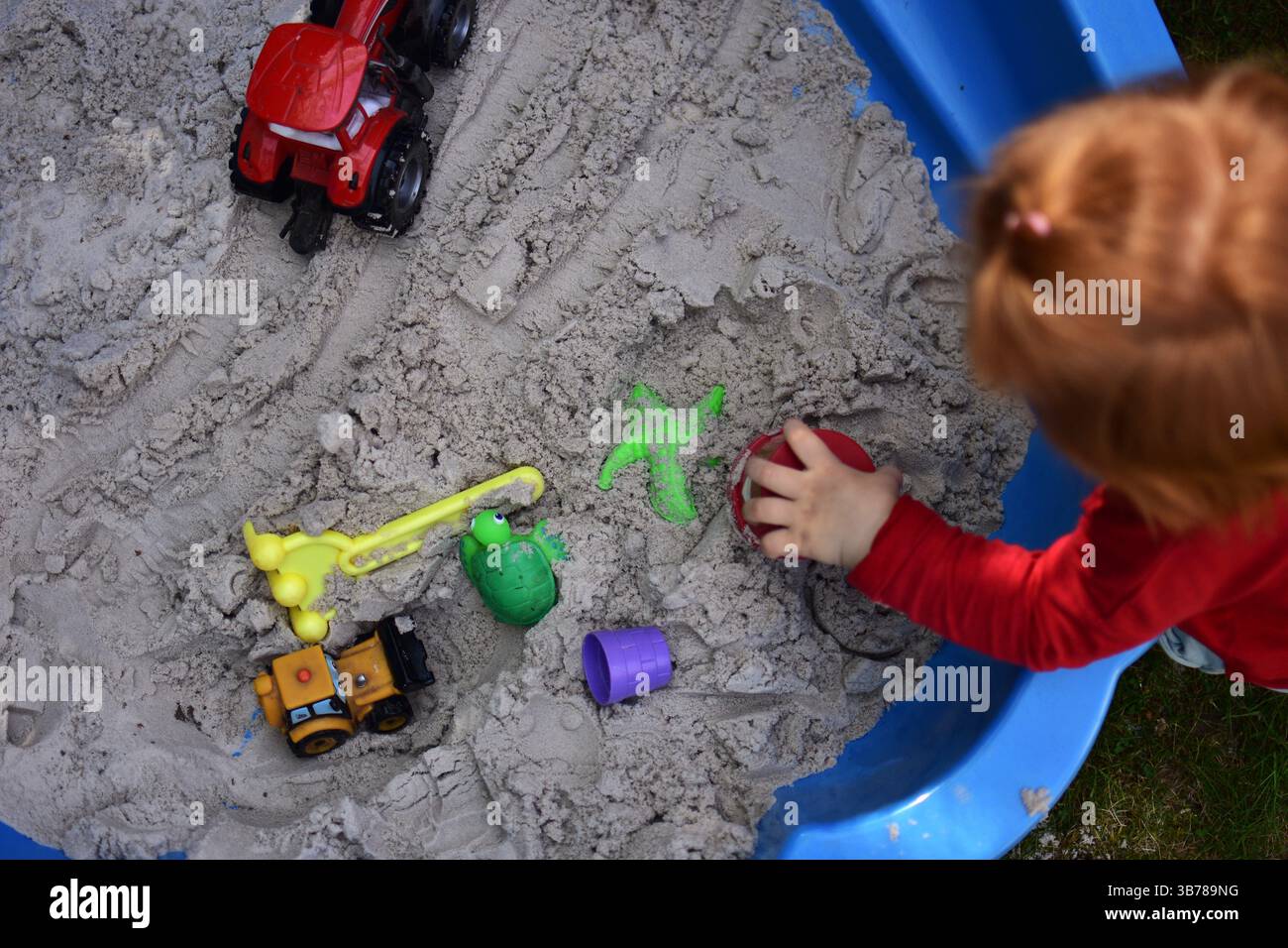 Toddler girl plays with sand toys in a small sandbox in a back yard top ...