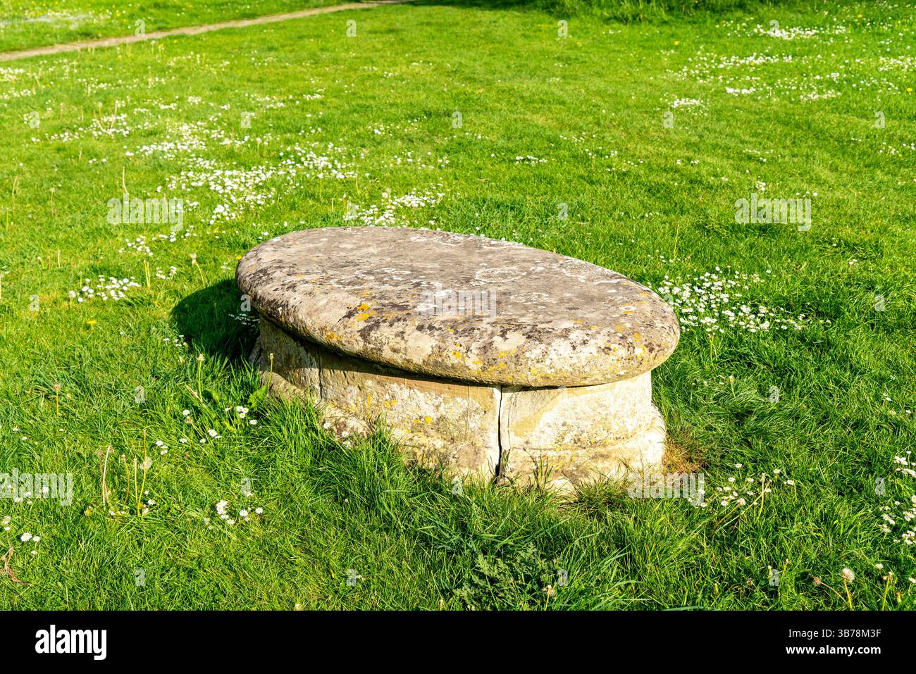 Oval shaped stone grave in a cemetery isolated in an area of green ...