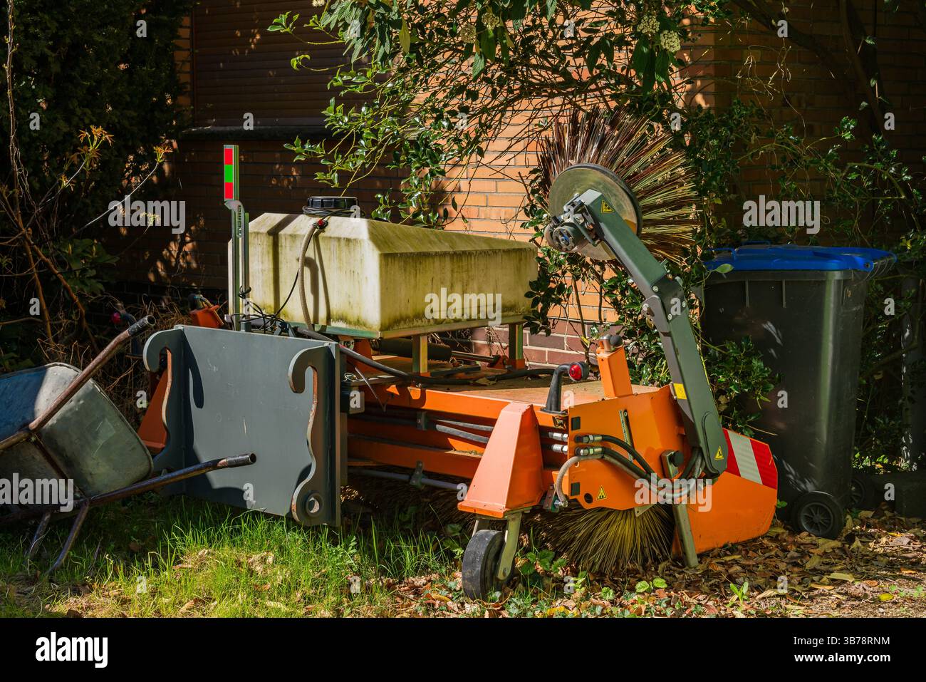 A landscaping machine sits idle in a garden surrounded by greenery. It ...